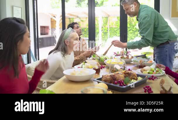 Diverse family sharing dinner with man spooning roast chicken at home ...