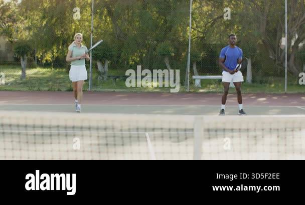 Doubles partners White woman and African American man tossing ball ...