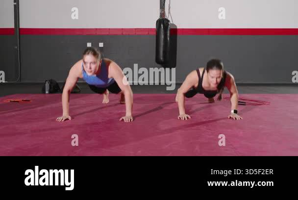Two women doing push-ups on red mat under punching bag when trainer ...