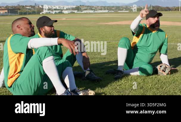 After pointing up Diverse male teammates sitting on outfield grass ...
