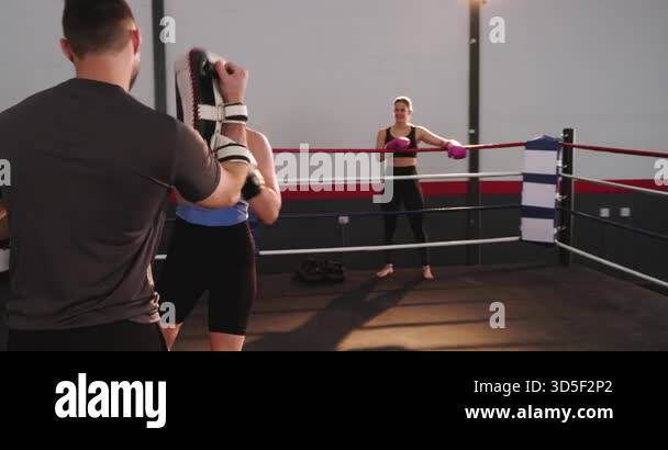 Coach holding focus pads for reach in boxing ring, white woman throwing ...
