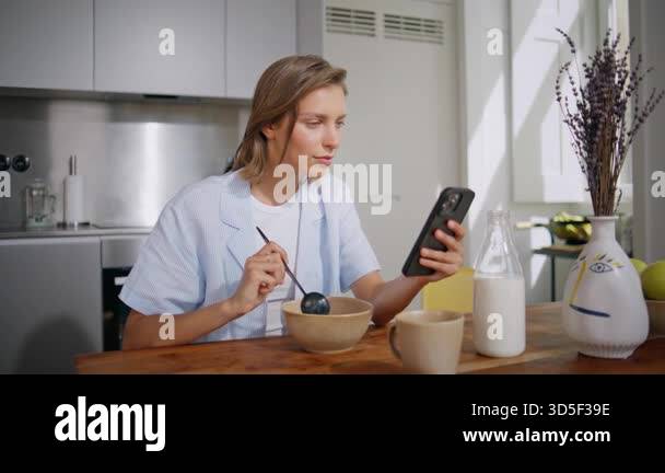 Eating woman texting sms in modern kitchen closeup. Smiling girl ...