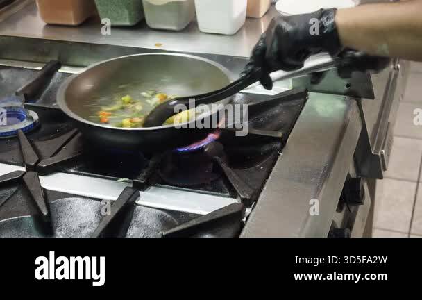 Professional chef carefully mixing colorful vegetables in metal pan ...