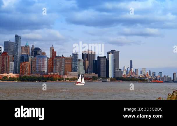 Lovely white sailboat moves by the river along New York skyline. Grey ...