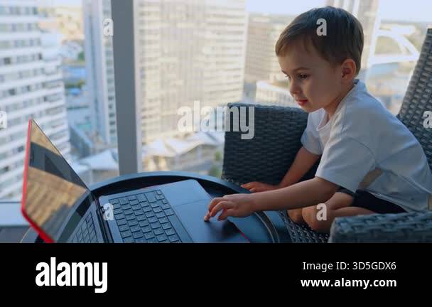 Beautiful Caucasian child is focused on the laptop. Baby boy touches ...