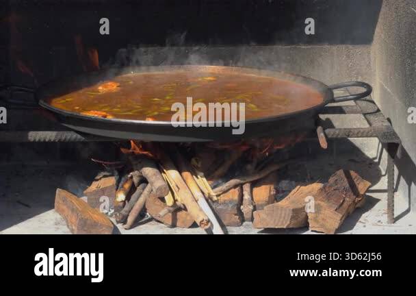 Cinematic slow-motion of traditional paella cooking outdoors: golden ...