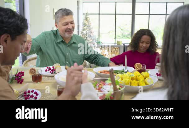 Father leading blessing at dining table by Christmas tree, family ...