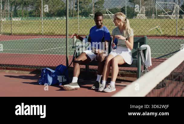 Walking off court Diverse tennis partners sharing phone on courtside ...