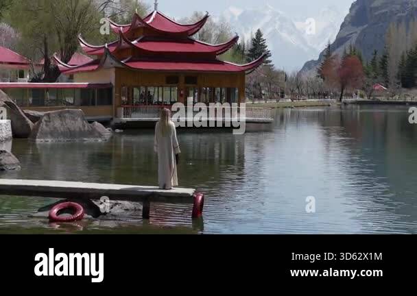 A serene lakeside scene in Pakistan, featuring a traditional pavilion ...