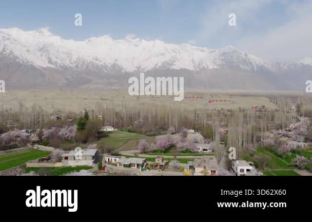 Aerial view of a serene village in Pakistan, surrounded by snow-capped ...