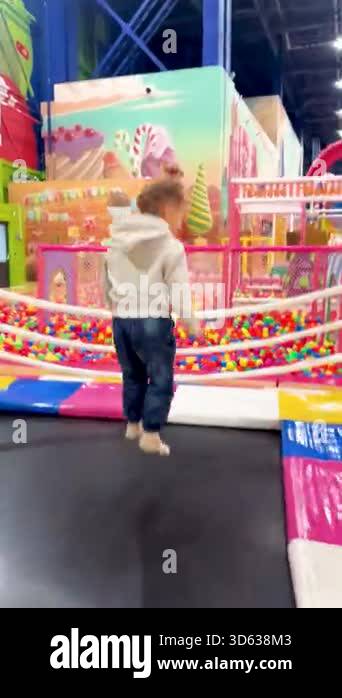 Cute toddler girl bouncing on trampoline in indoor kids arena. Active fun, family leisure and ...