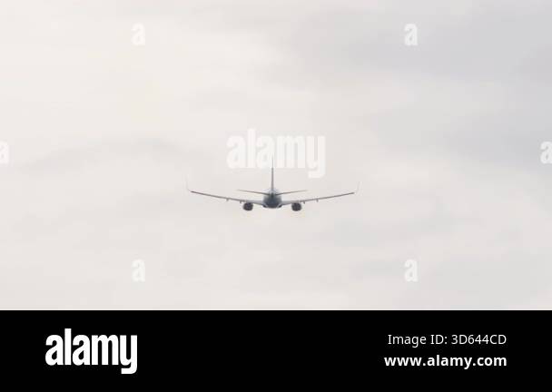 Back view of a commercial airliner climbing into the cloudy sky after ...