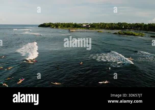 Surfers ride waves near reef while pier and hut stretch from shore ...