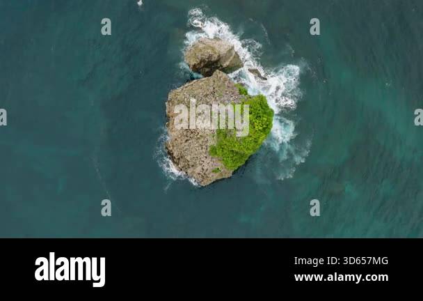 Rock islet covered with green vegetation surrounded by waves in deep ...