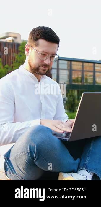 Young male freelancer working computer at modern glass building ...