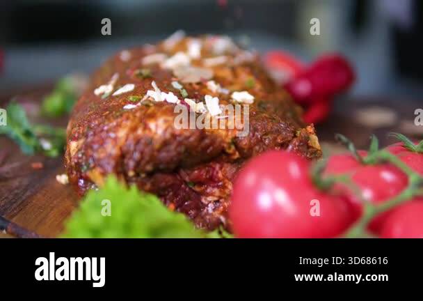 A man sprinkles spices on chicken fillet. Filmed on a high-speed camera ...