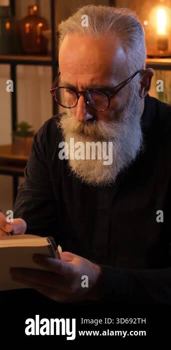 Close-up of a focused senior man with a beard and glasses writing notes ...