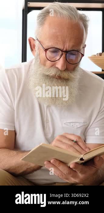 Close-up of a thoughtful senior man with a beard reading a book ...