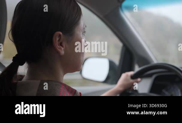 Over the shoulder view of a young woman with dark hair driving a car ...