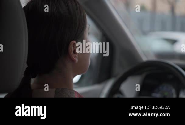 Over the shoulder view of a young woman with dark hair driving a car ...