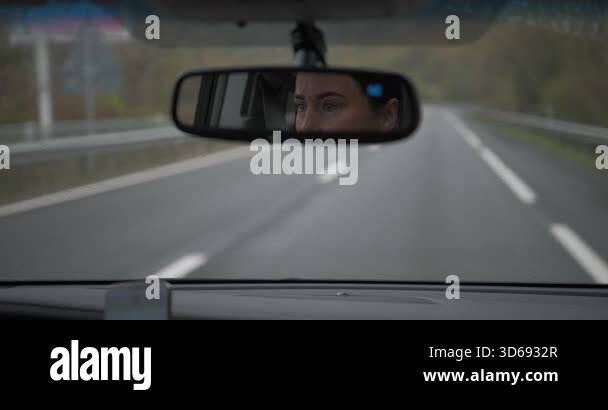 Close-up view of a young womans eyes and face reflected in the rearview ...