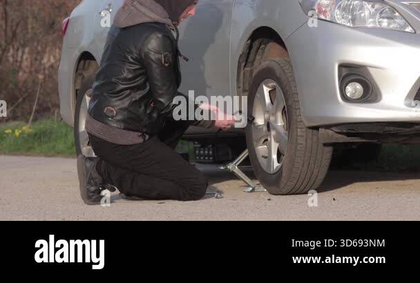 Changing wheel on car, spare tire by the roadside, unscrewing lug nut ...