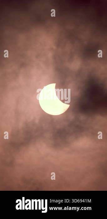 Vertical view of a partial solar eclipse hidden behind golden clouds ...