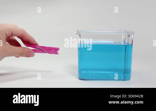 A hand drops a pink clothes peg into blue water, observing its buoyancy ...