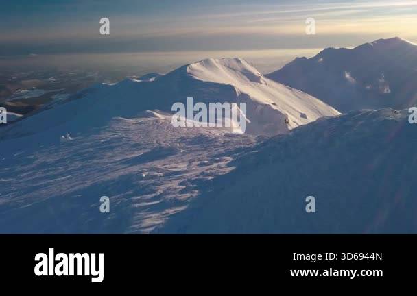 Stunning aerial footage of a frozen alpine ridge bathed in warm sunset ...