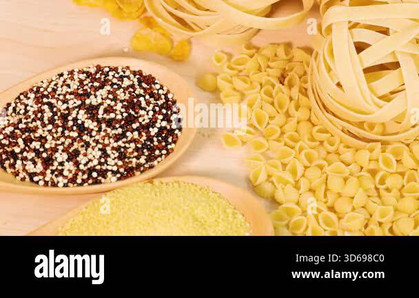 Various pasta types and grains arranged on a light wooden background ...
