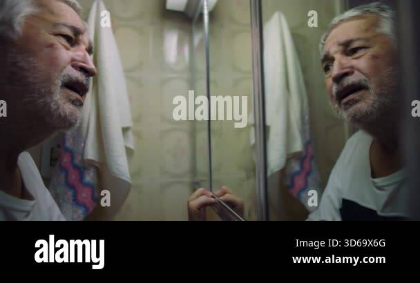 Older man raising hands in front of mirror, mouth open in shock and ...