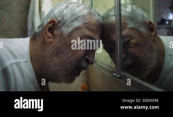 Older man resting forehead against mirror, eyes closed, expressing ...