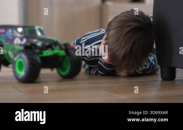Little boy lying on wooden floor playing quietly with toy monster truck ...