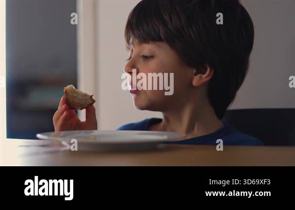 Child taking big bite of bread during breakfast at table, showing ...