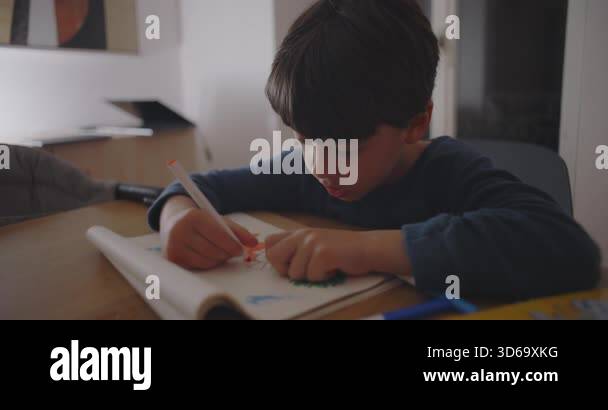 Young boy deeply focused drawing in sketchbook with colorful markers at ...