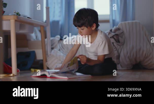 Boy studying book with focus while sitting cross legged on floor at home, child development ...