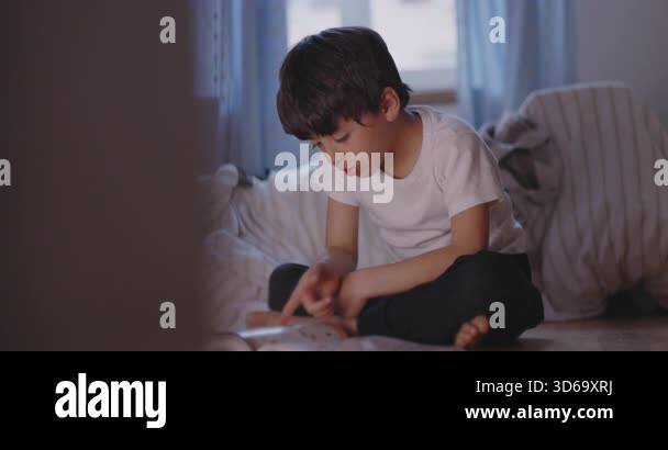Boy sitting on bedroom floor reading book with focus, child ...