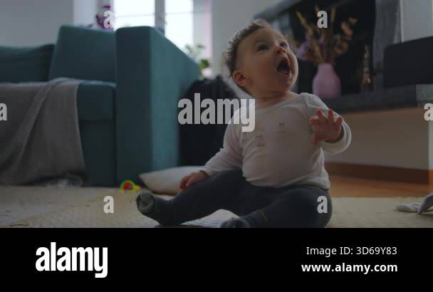 Baby sitting on floor laughing joyfully, mouth open in wide smile ...