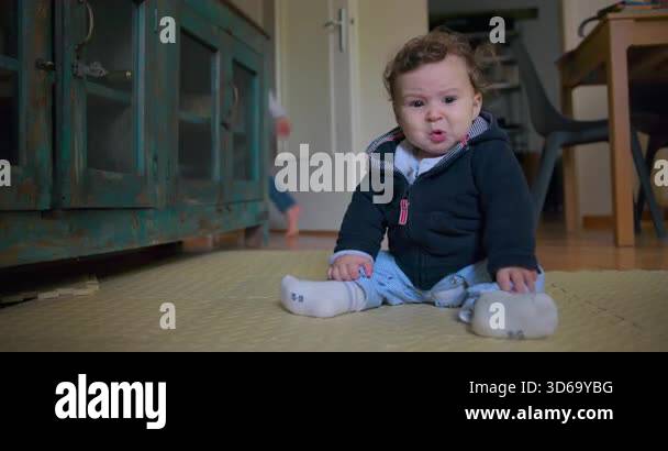 Baby sitting on play mat looking down with curious expression, early ...