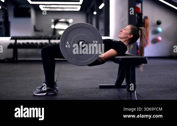 A woman performs a glute bridge with weights in a stylish gym. The ...