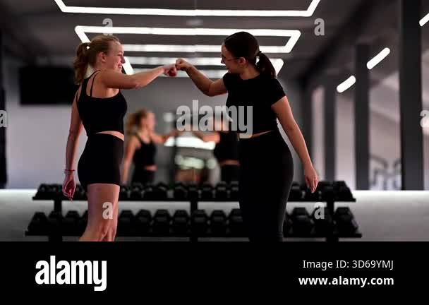 Two friends are exercising in a contemporary gym, smiling and ...