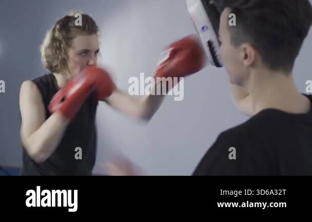 Strong athletic female in boxing gloves makes punches on paw held by ...