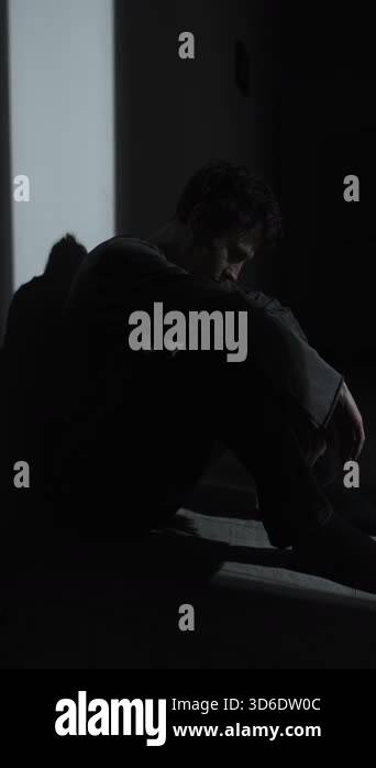 Man sitting on the floor in a dark room, holding his head in silent ...