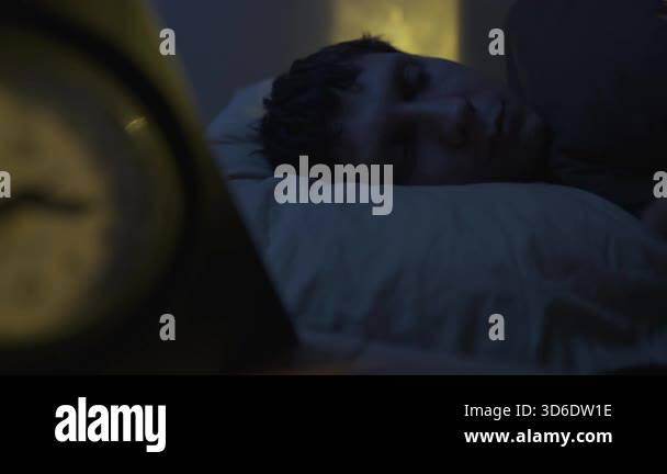 Man turning in bed unable to sleep, warm yellow streetlight through ...