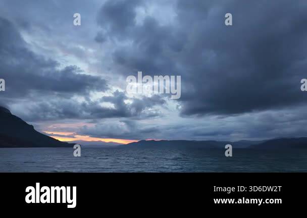 Sunrise behind storm clouds over sea and mountains time-lapse of ...