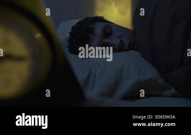Young man lies awake at night, staring with open eyes. Blurry clock in ...