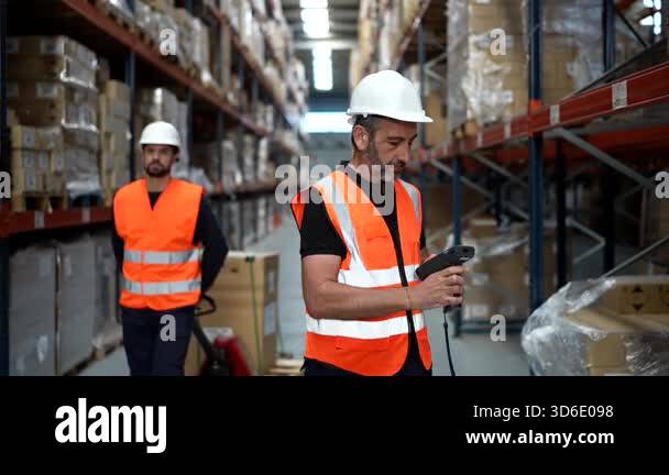 Logistics manager in a helmet and safety vest using a handheld barcode ...