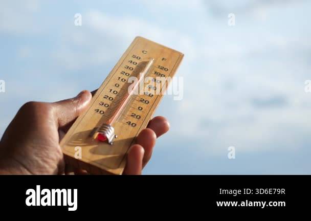 A person holds a thermometer to check the weather conditions outside ...