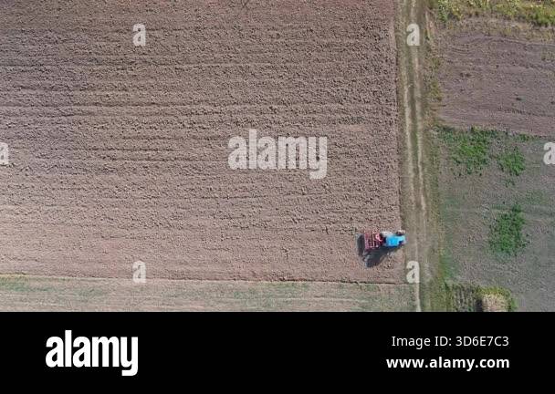 Aerial vertical shot of a blue tractor working on farmland, creating ...