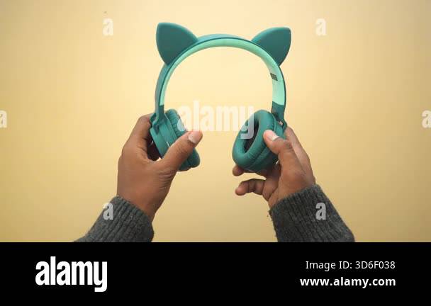 Two hands hold playful cat ear headphones against a warm background ...